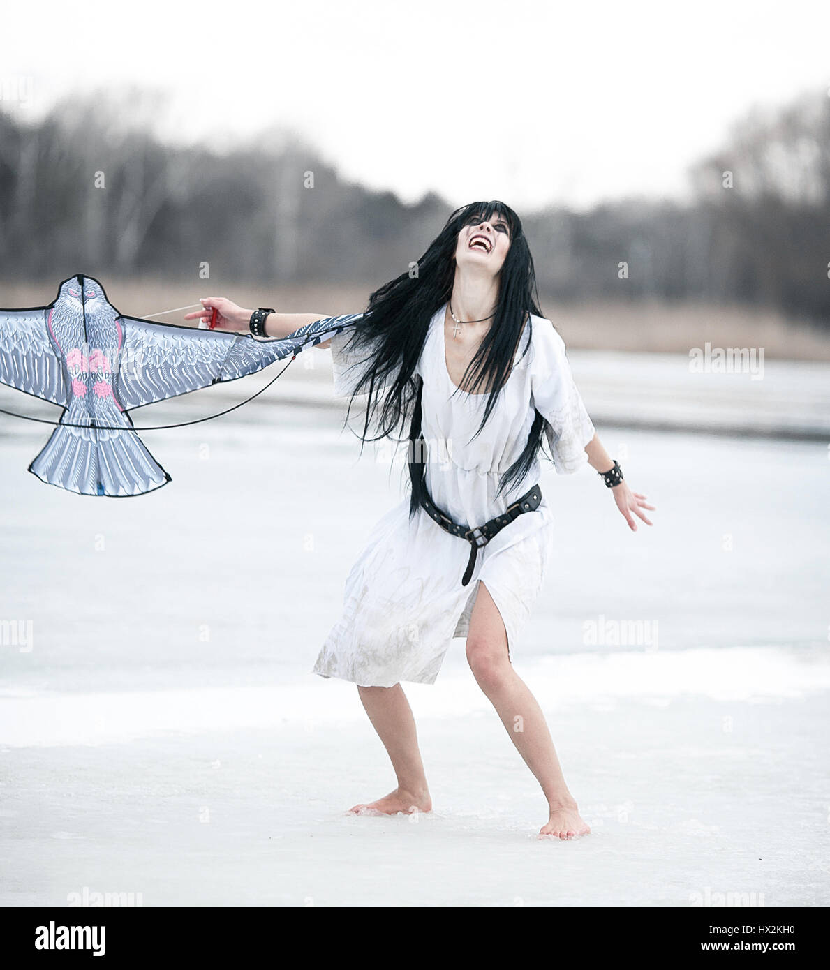 Crazy young woman standing on ice lake with kite in her hand. She is ...