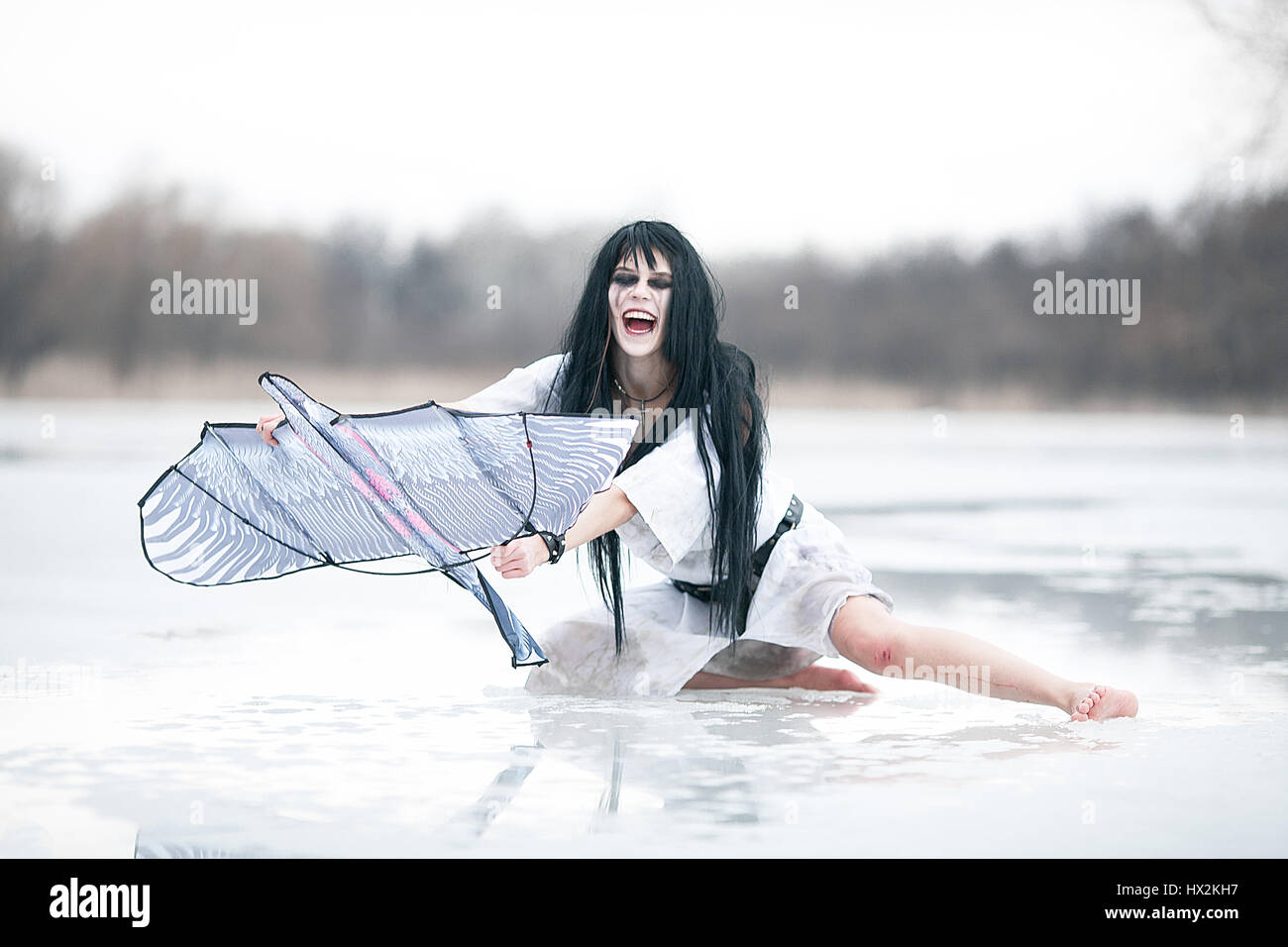 Crazy young woman sitting on ice lake with kite in her hand. She is ...