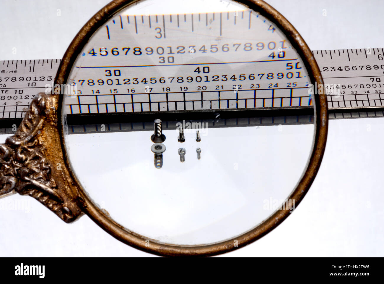 small screws with ruler on mirror with magnifying glass Stock Photo - Alamy