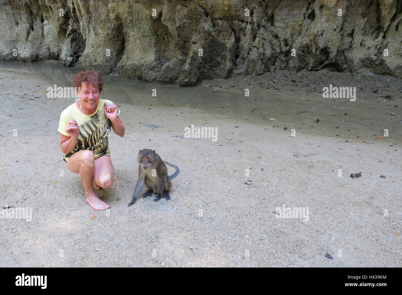 A close up shot af a tourist with monkey on a sandy beach on Panak ...