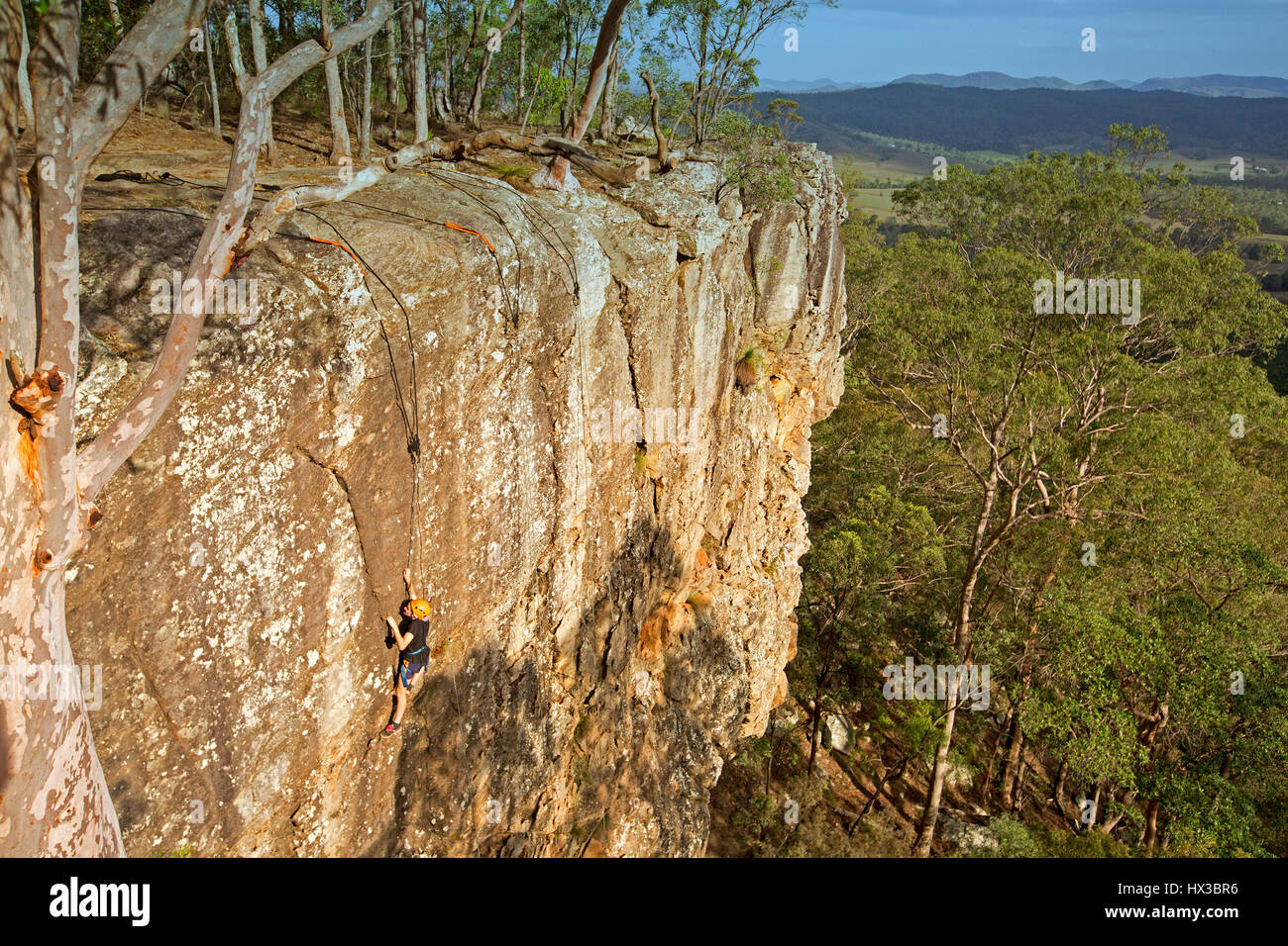 A teenage girl climbing up a high cliff face with extensive view of ...