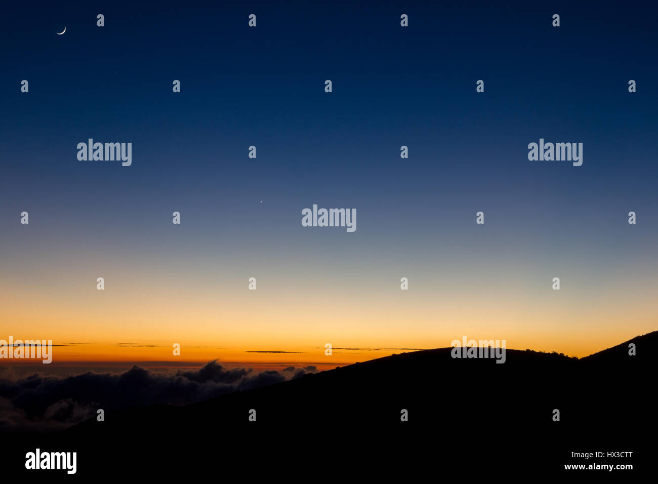 Crescent moon over the bright orange horizon lit by the last light of ...