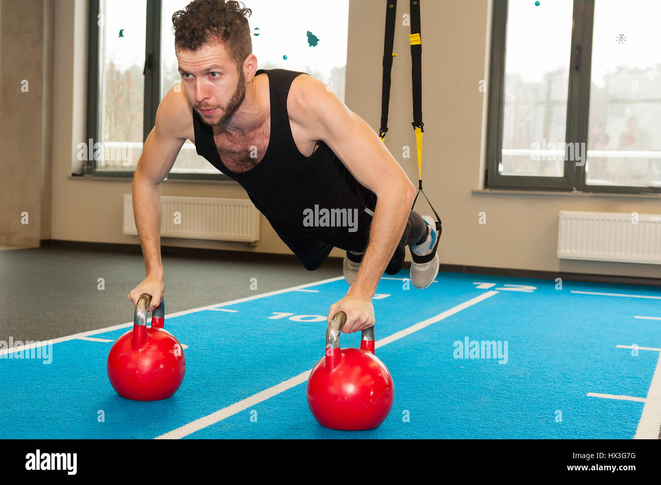 white curly bearded sporty man exercising with fitness straps in gym ...