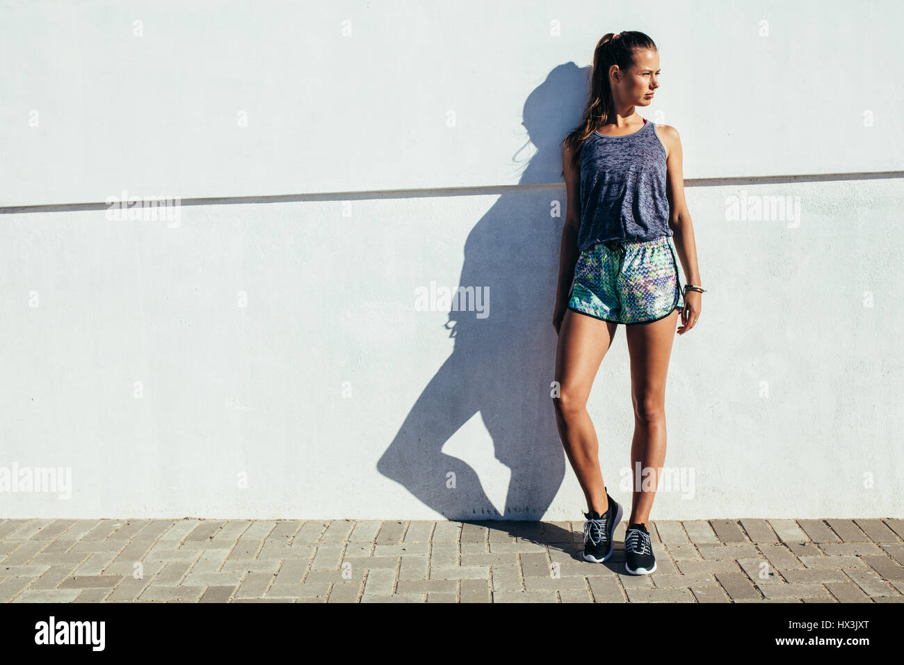 Full length shot of healthy young female leaning to a wall outdoors and ...
