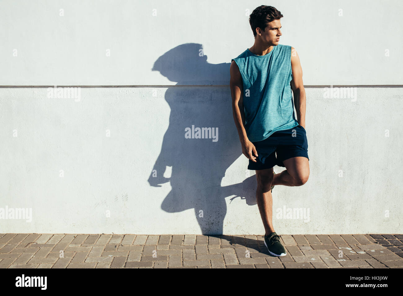 Full length shot of healthy young male runner leaning to a wall ...