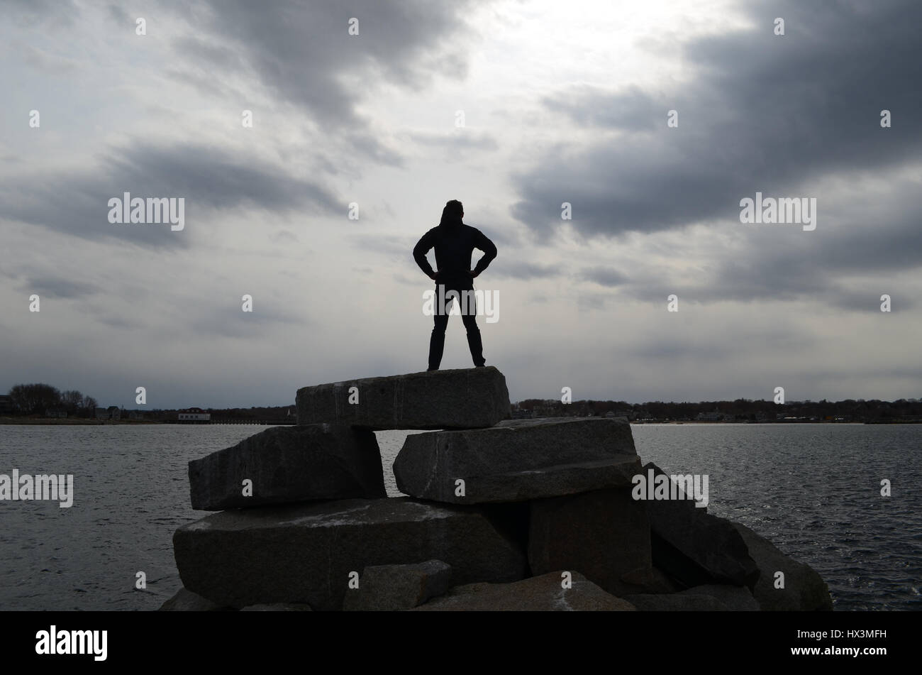 Guy silhouetted againsta stormy sky in a super hero pose on a rock ...