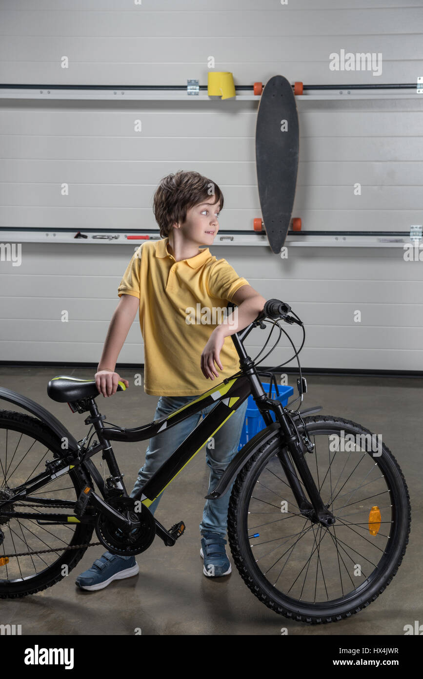 Cute little boy standing with bike and looking away in workshop Stock ...