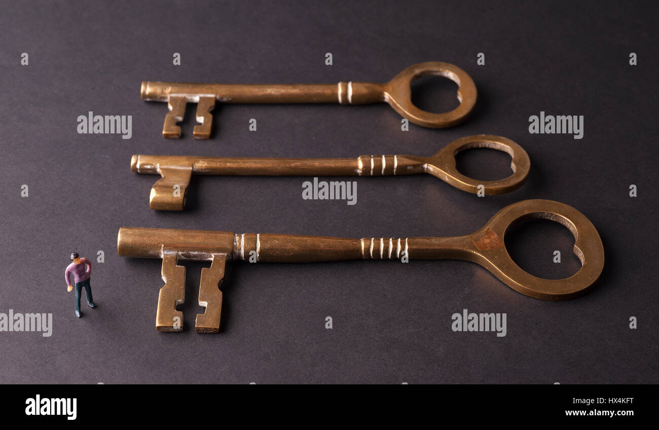 Miniature figure standing beside three giant brass keys on dark ...