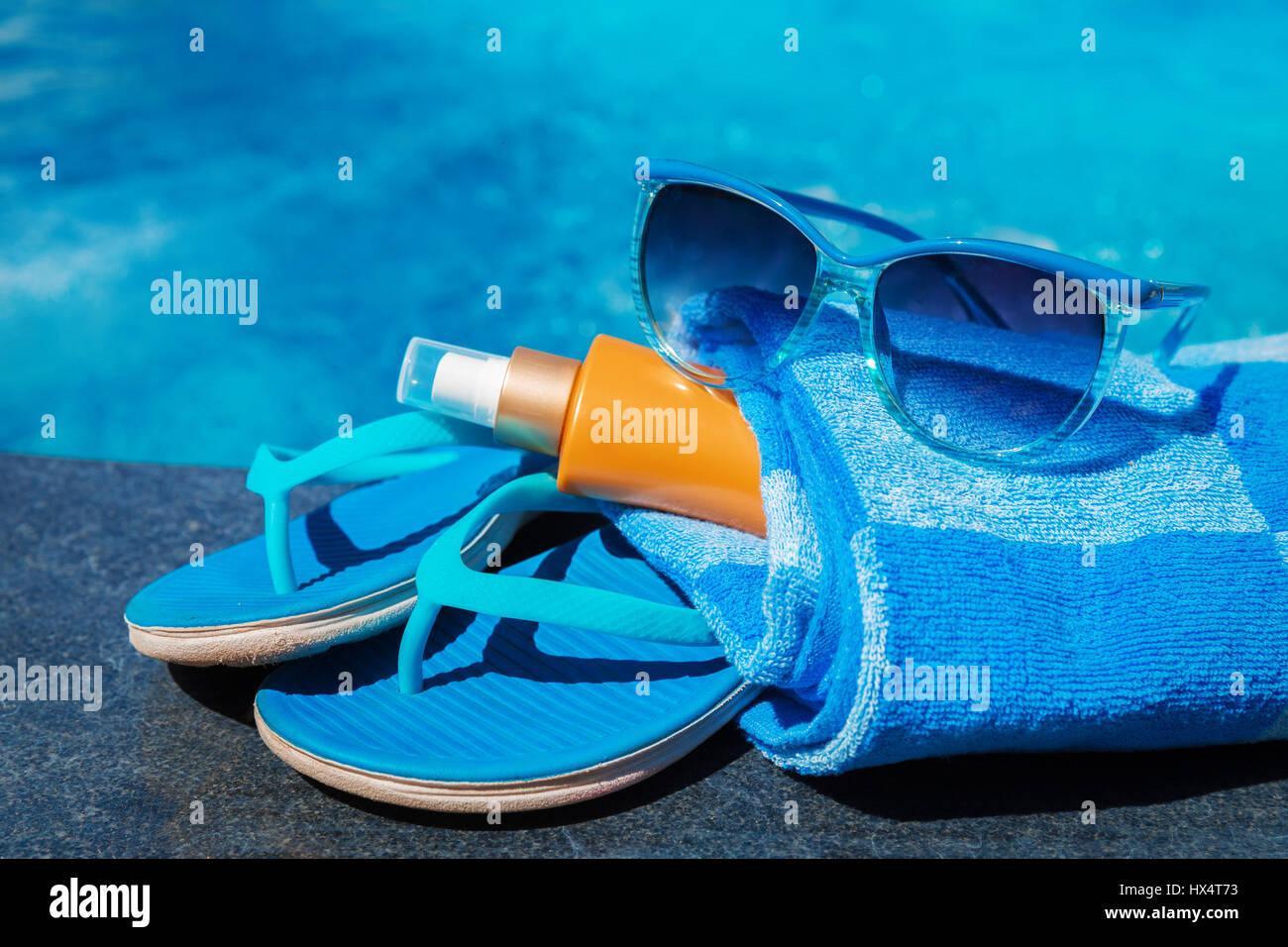 Blue slippers, sunsscreen cream and sun glasses near swimming pool ...