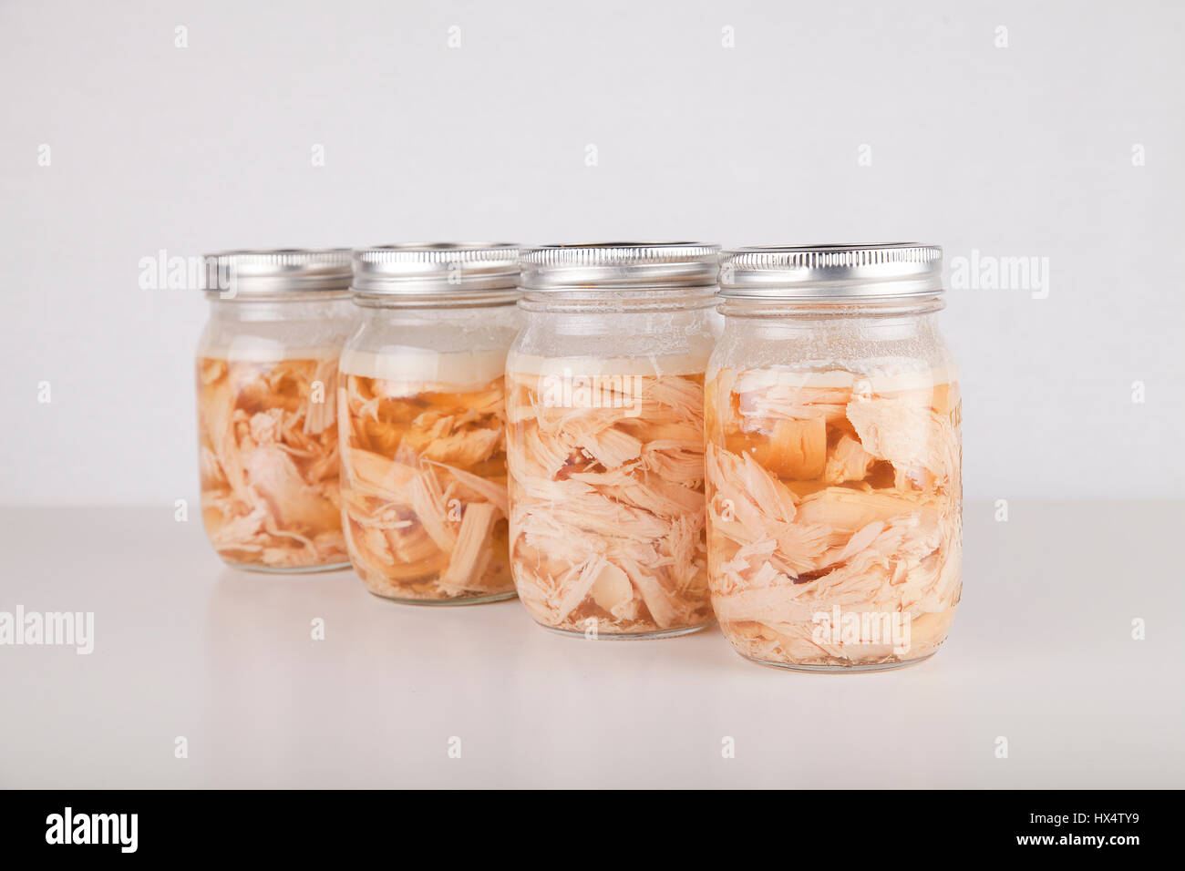 Jars of homemade cooked chicken on a white surface. Food cans isolated ...