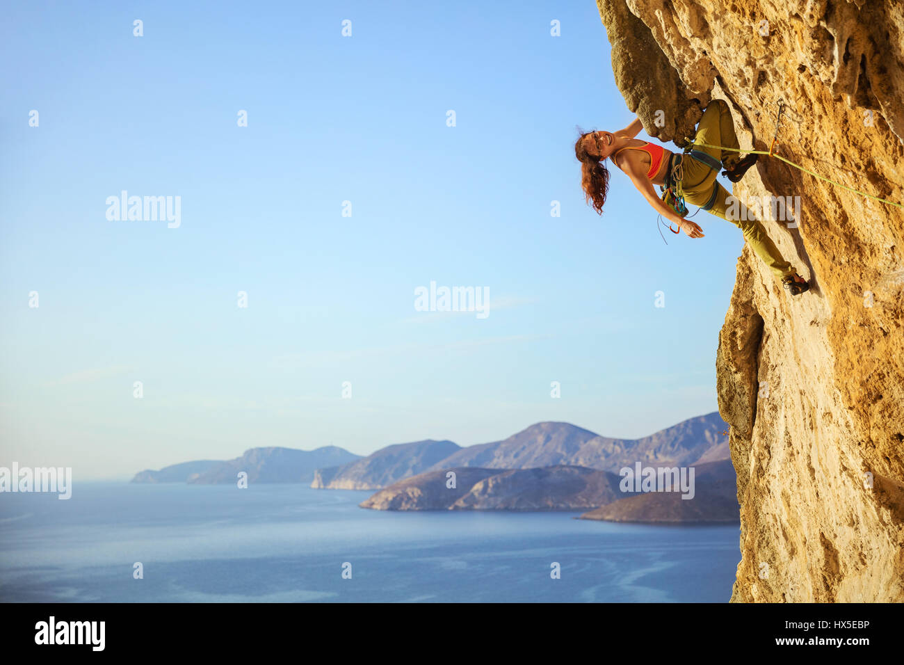 Young female rock climber gripping calanet with one hand and smiling ...