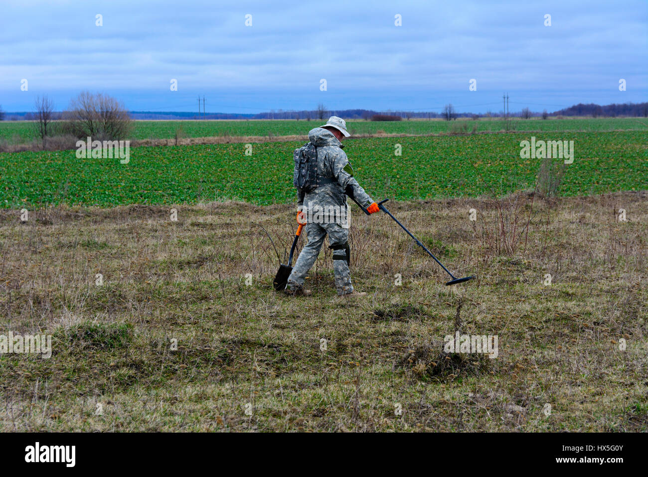 Man with a device for finding treasures with a shovel on the field ...