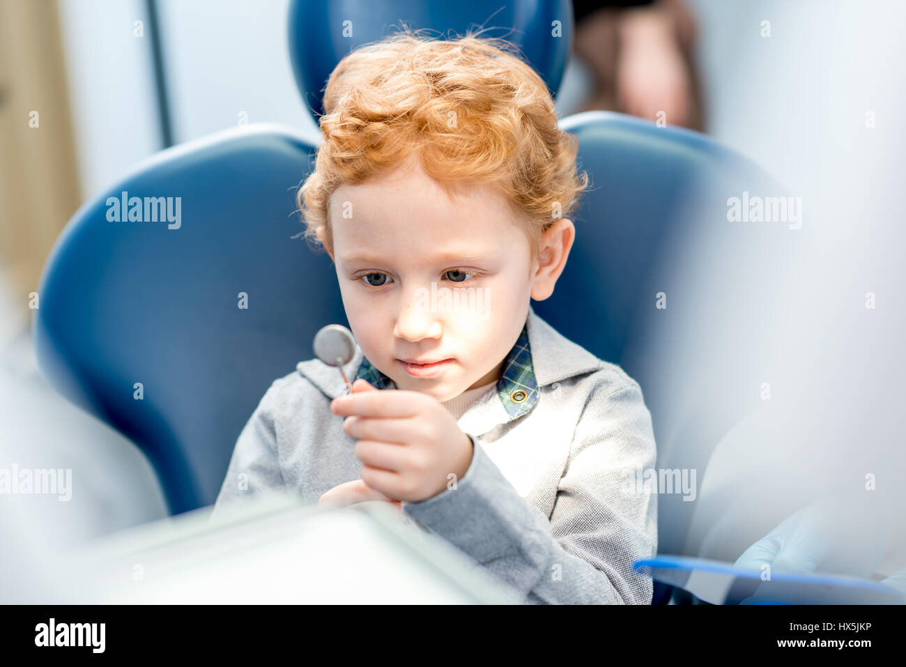 Young excited boy looking at the dental mirror sitting on the chair at ...