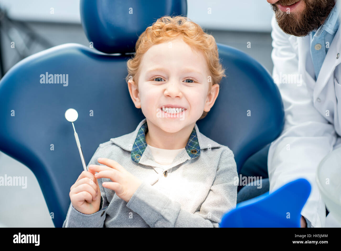Young excited boy looking at the dental mirror sitting on the chair at ...