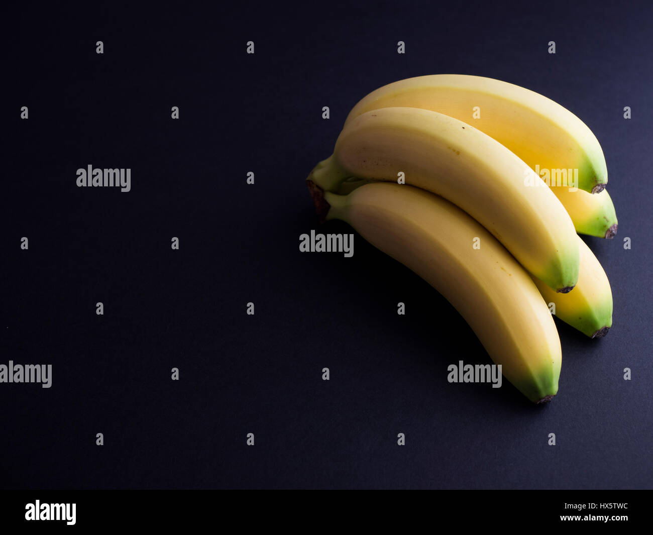 Bunch of small bananas isolated on dark background Stock Photo - Alamy