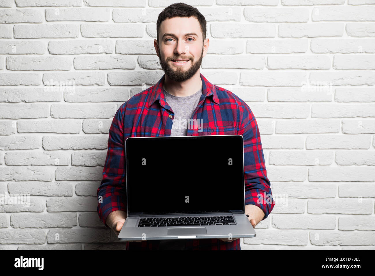 Happy young man show laptop with screen against brick wall Stock Photo ...