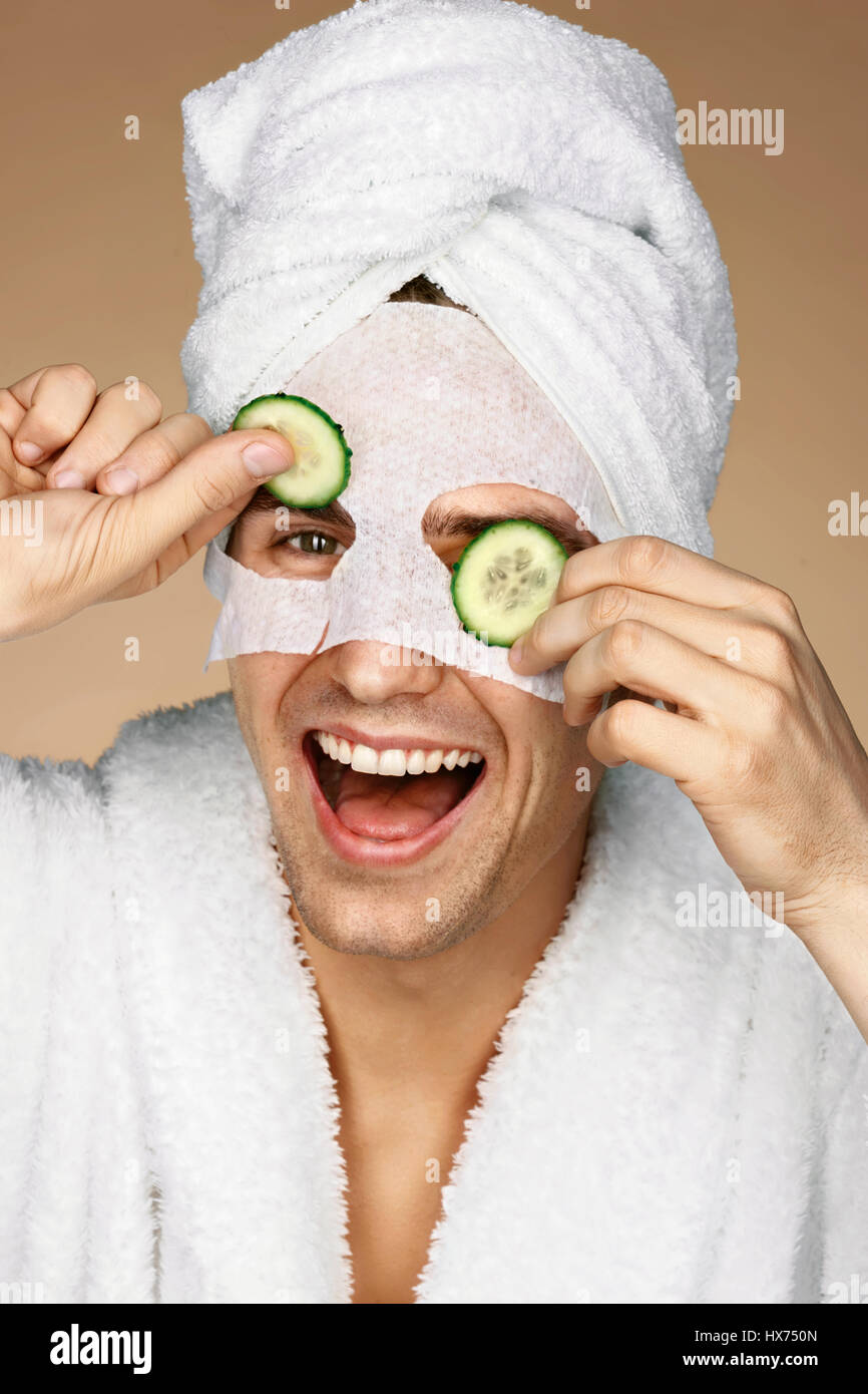 Smiling man wears cotton mask and holding slices of cucumbers. Photo of ...