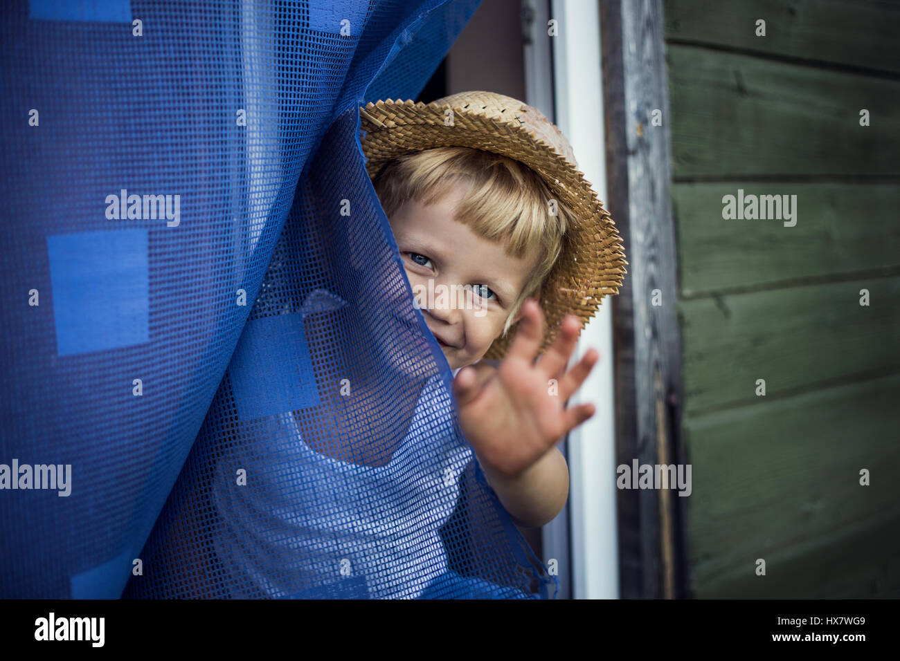 Outdoor portrait: Cheerful kid with straw hat leaning out a window ...