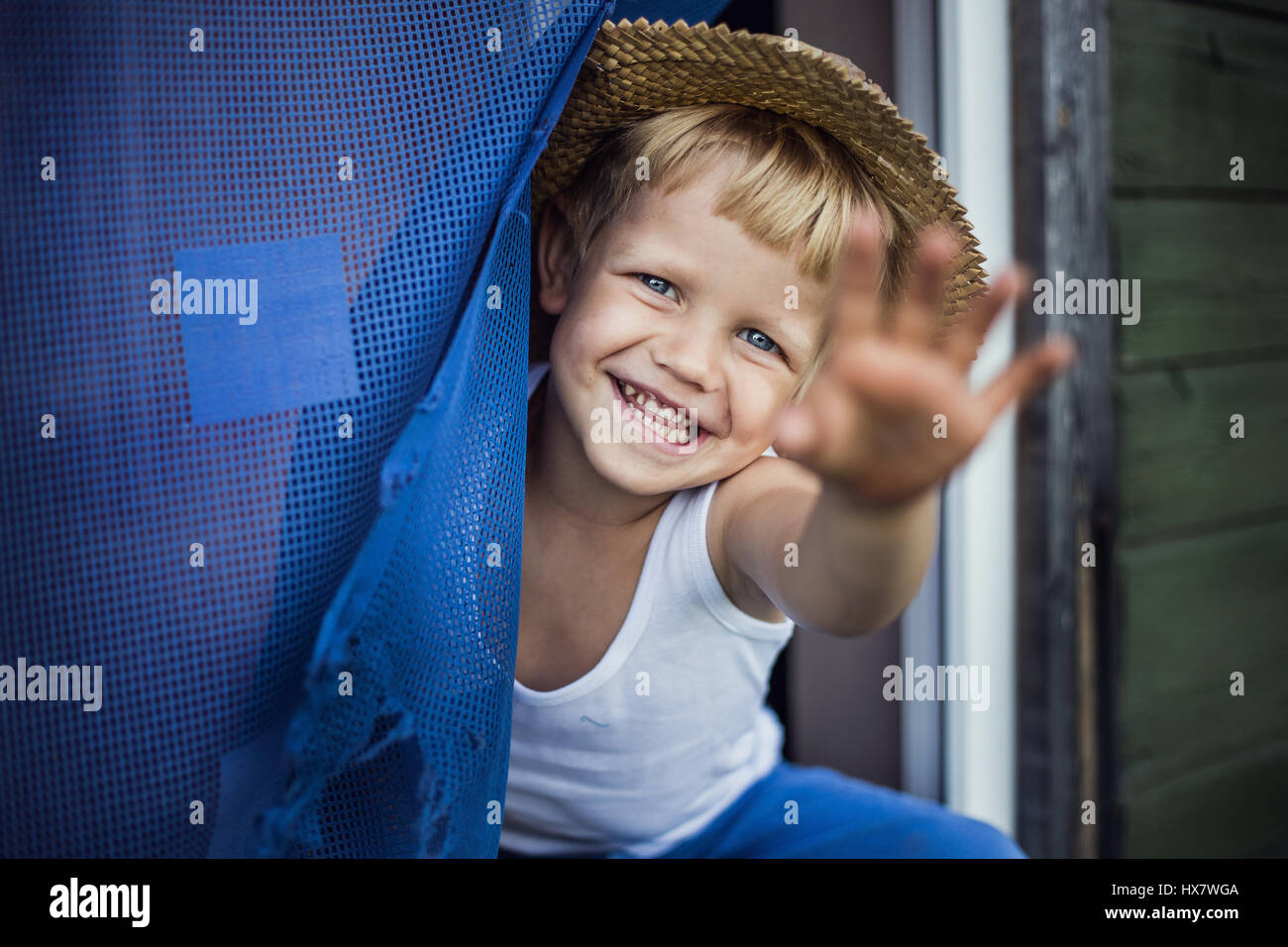 Outdoor portrait: Cheerful kid with straw hat leaning out a window ...