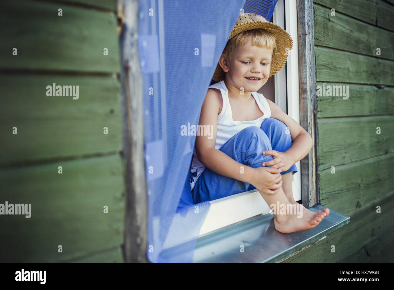 Outdoor portrait: Cheerful kid with straw hat leaning out a window ...