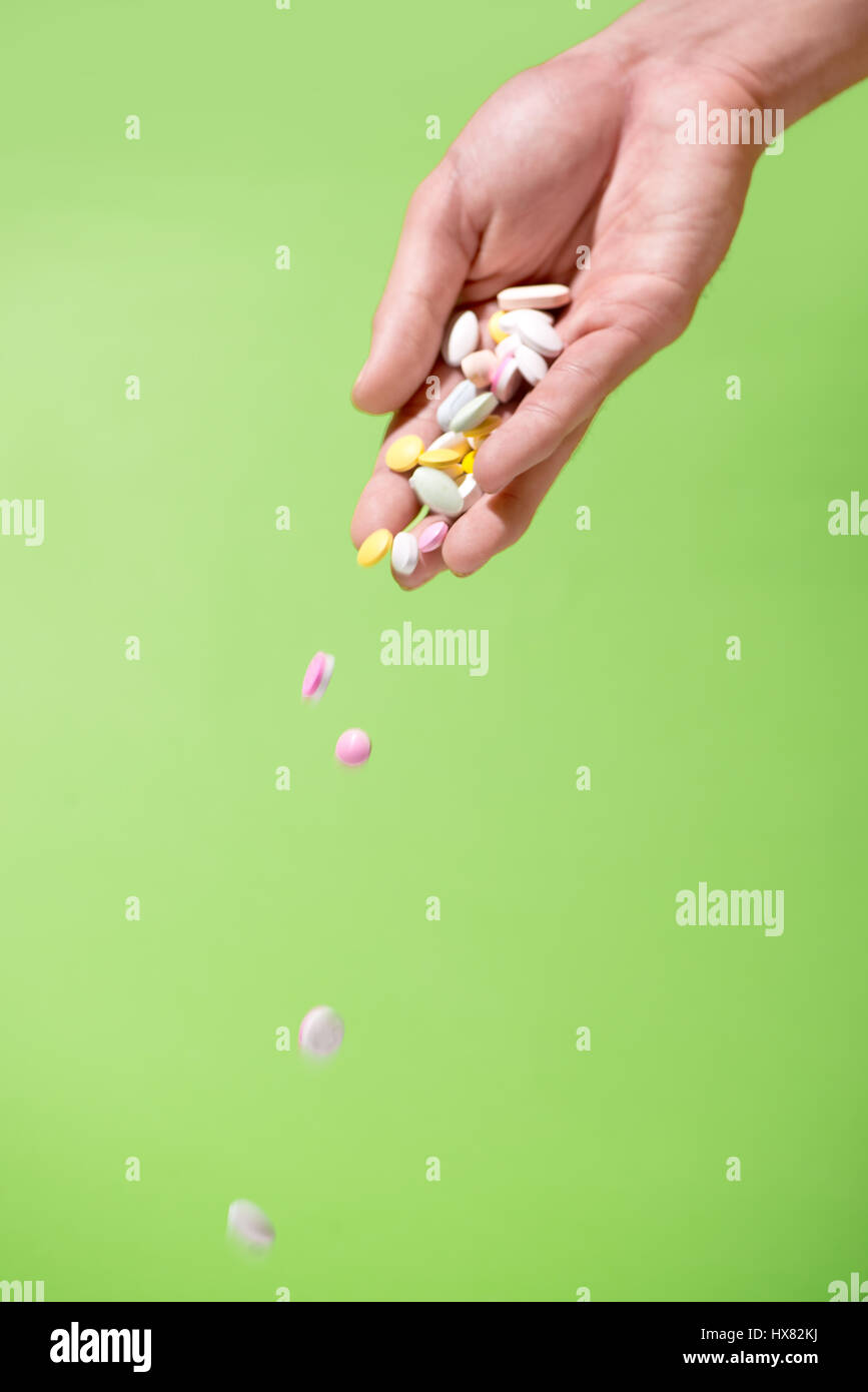 Colored pills falling from hand on green background Stock Photo - Alamy