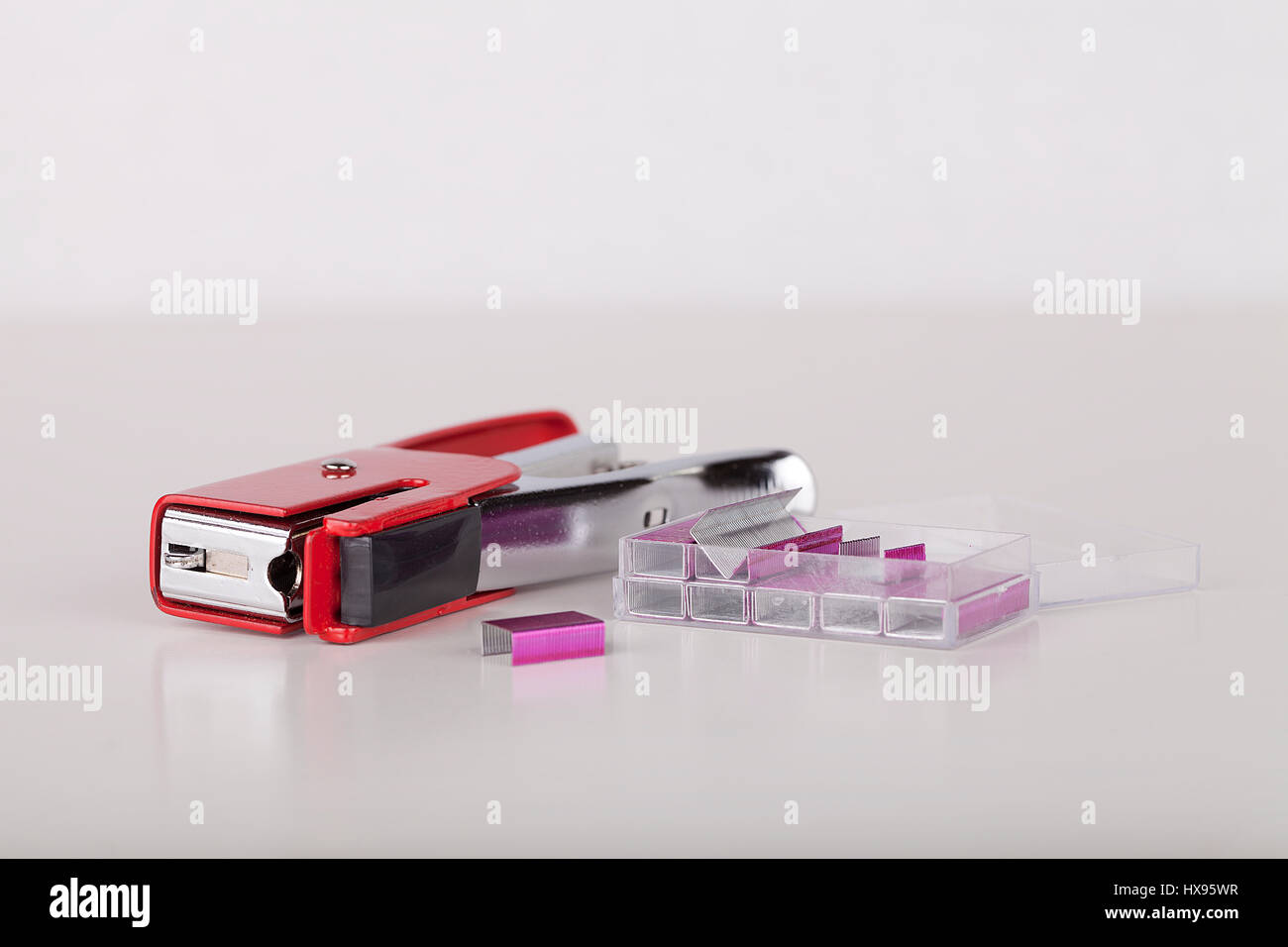 Red stapler with pink staples on a white surface. Stapler and staples ...