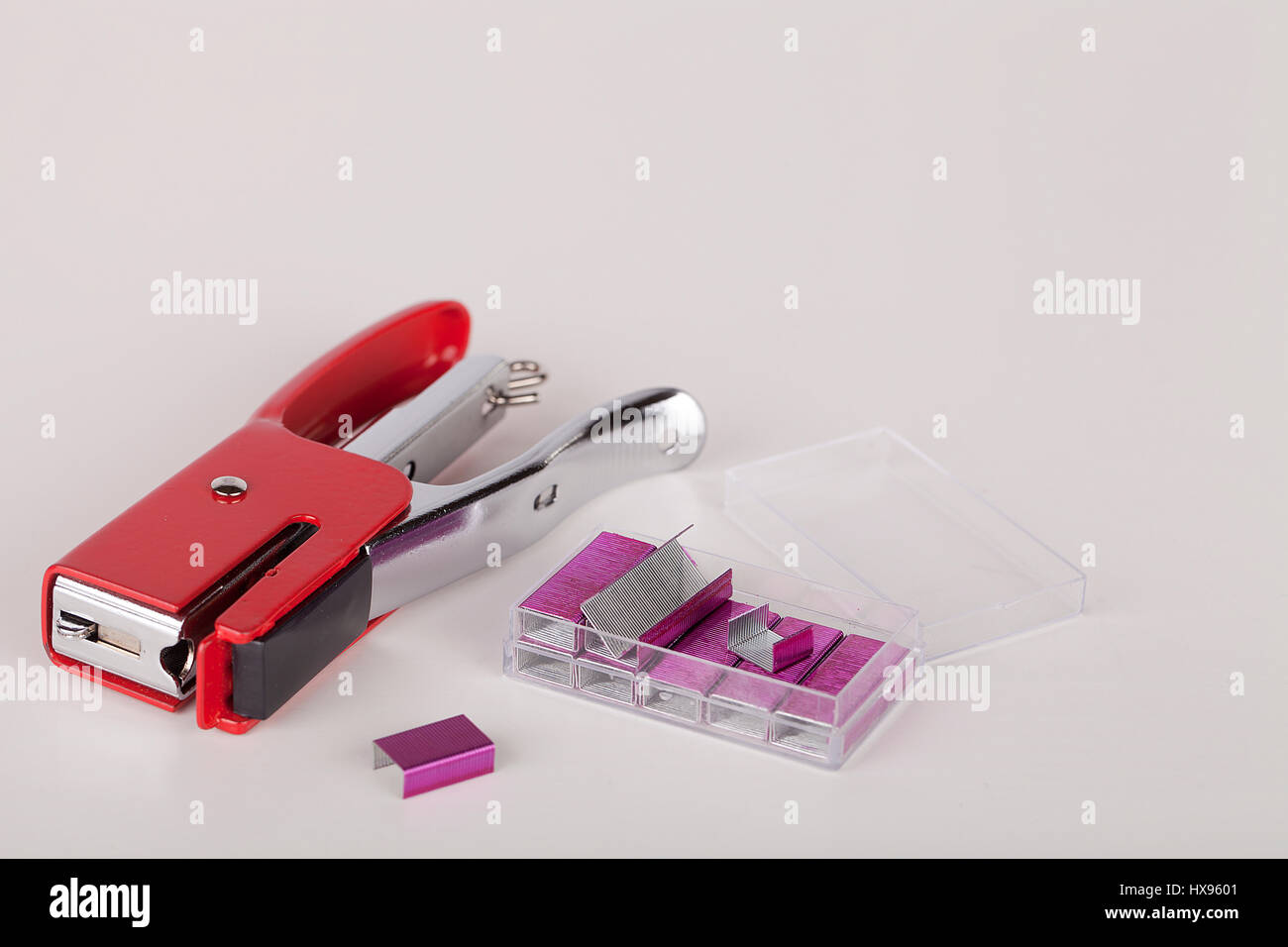 Red stapler with pink staples on a white surface. Stapler and staples ...