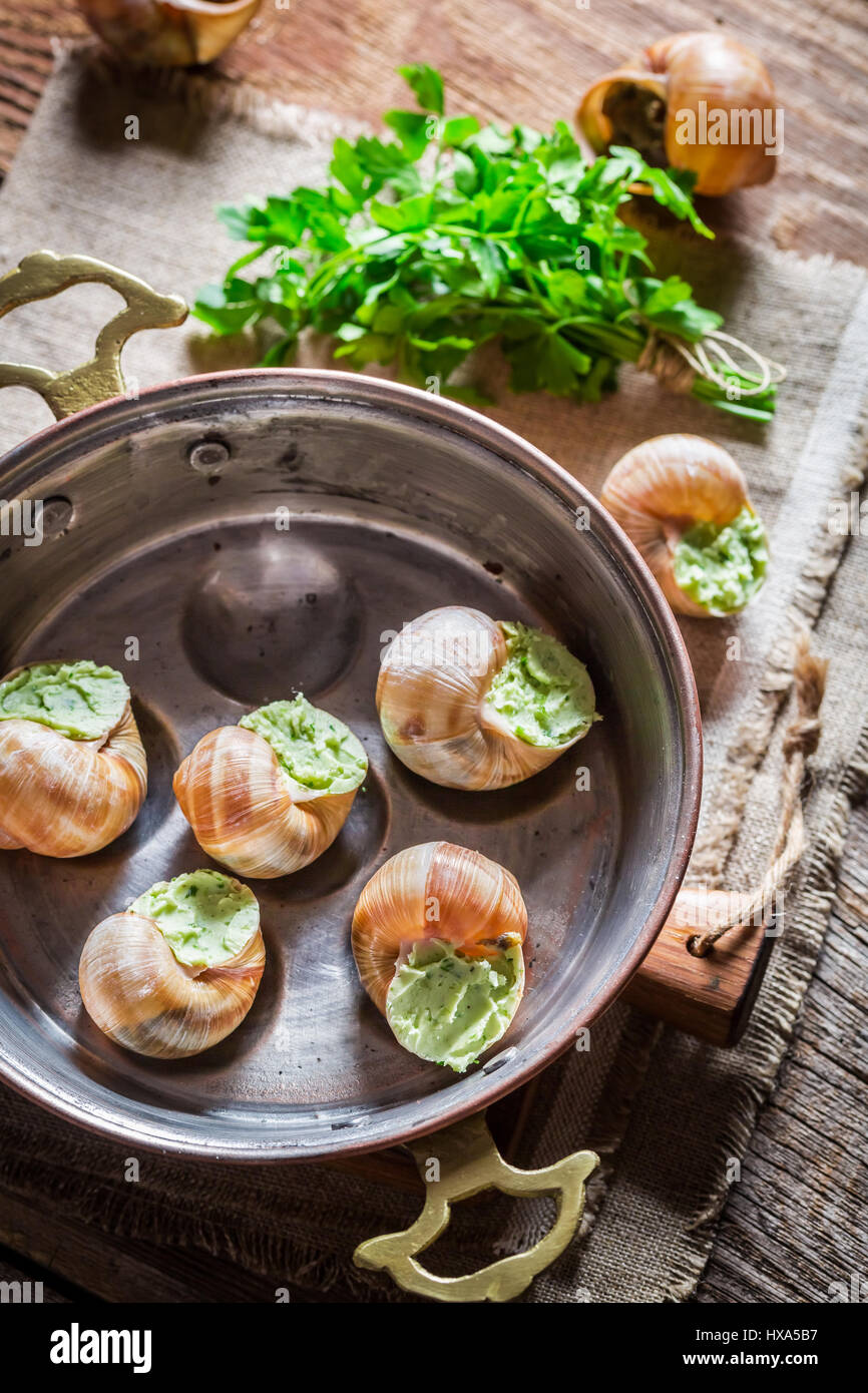 Delicious snails with garlic butter on old wooden table Stock Photo - Alamy