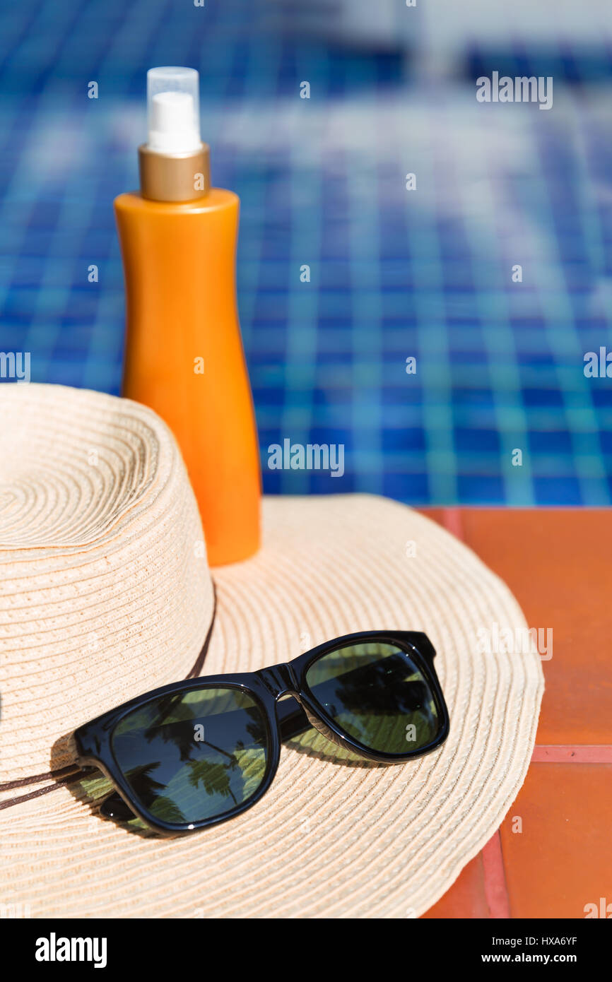Sunscreen cream and sun glasses with straw hat near swimming pool ...