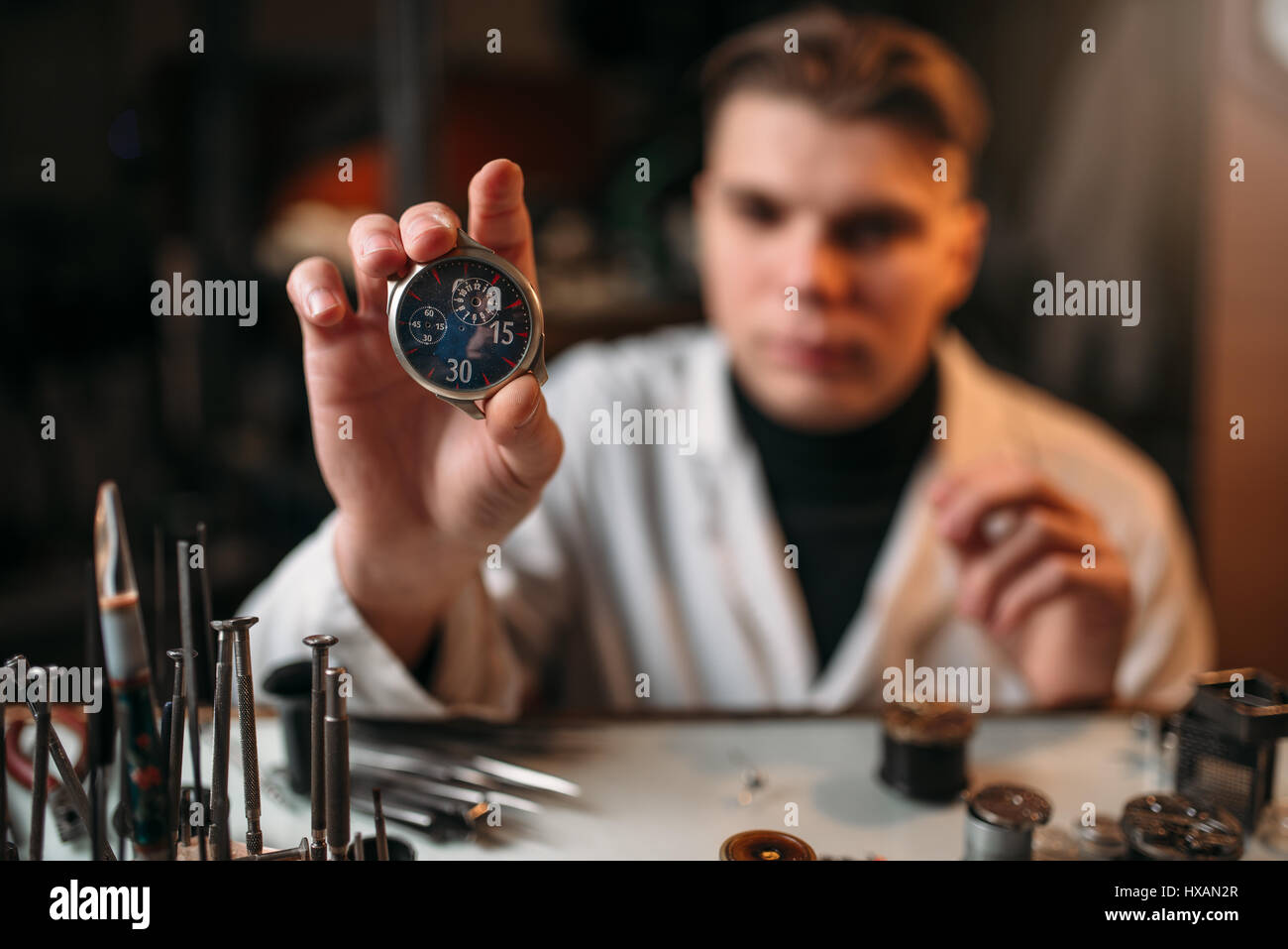 Watch maker holding wrist watch in hand. Watchmaking tools on the table ...