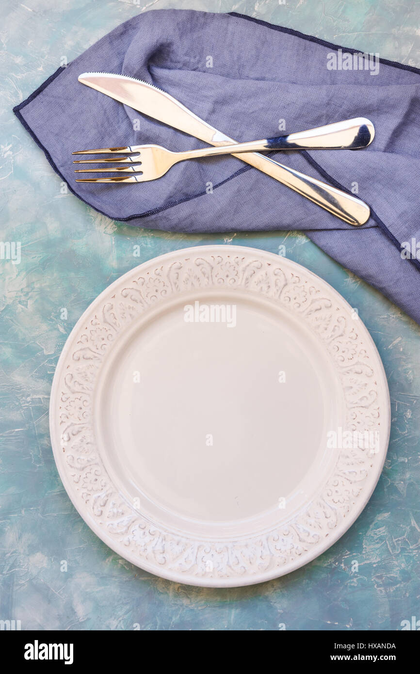 Empty table setting arrangement, white plate, cutlery, blue napkin ...