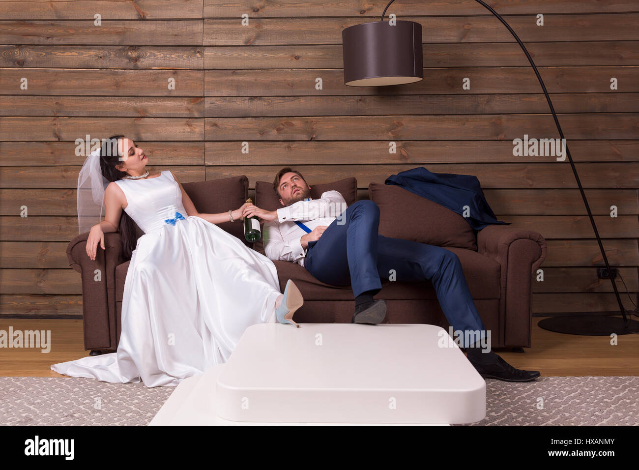 Drunk bride and groom relax on couch with bottle of alcohol after ...
