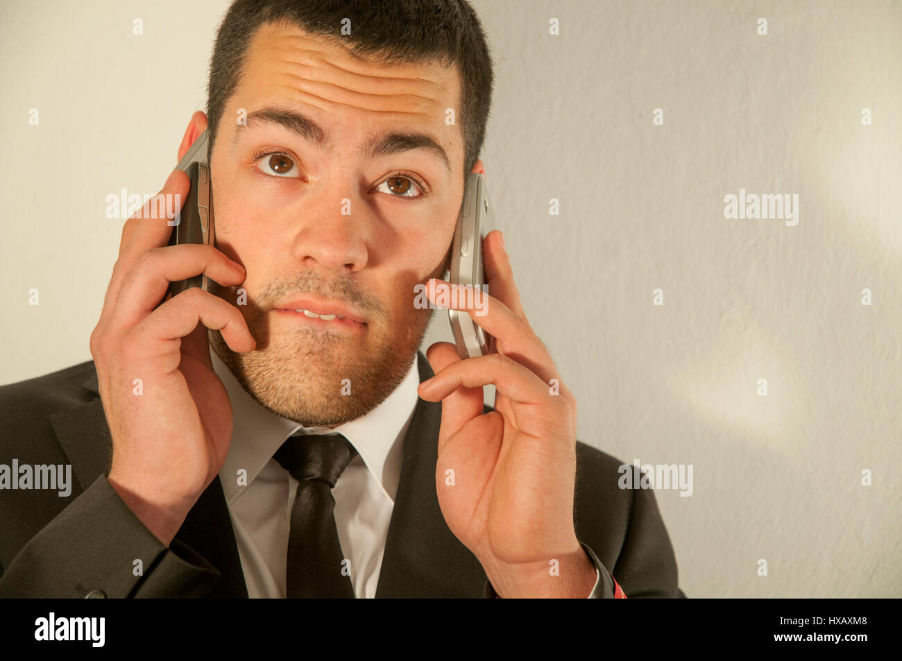 Young man using two mobile phones and bitting his lip Stock Photo - Alamy