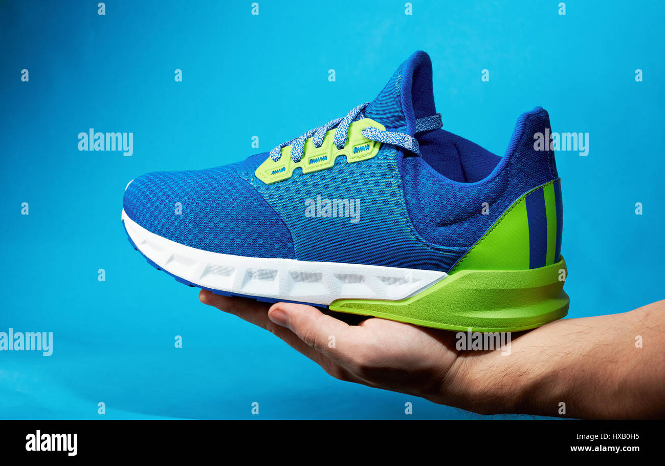 Hand hold one running colorful shoe isolated on blue background close ...
