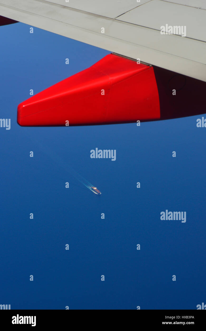 Aerial view of an airplane's wing detail as it flies over blue water ...