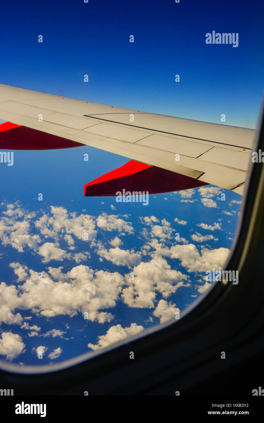 A plane wing in foreground with dramatic white clouds and blue sky as ...