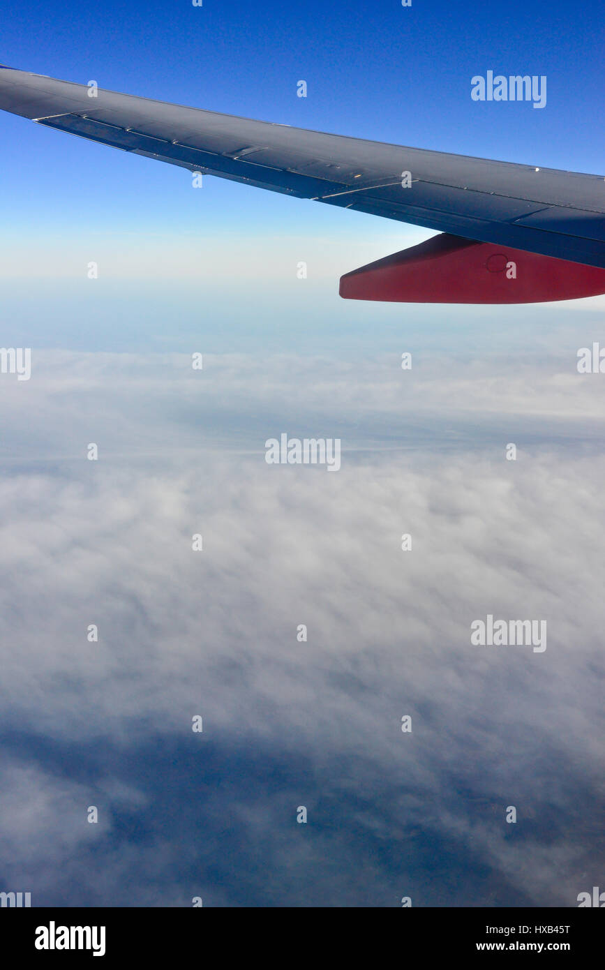 A plane wing in foreground with dramatic white clouds and blue sky as ...