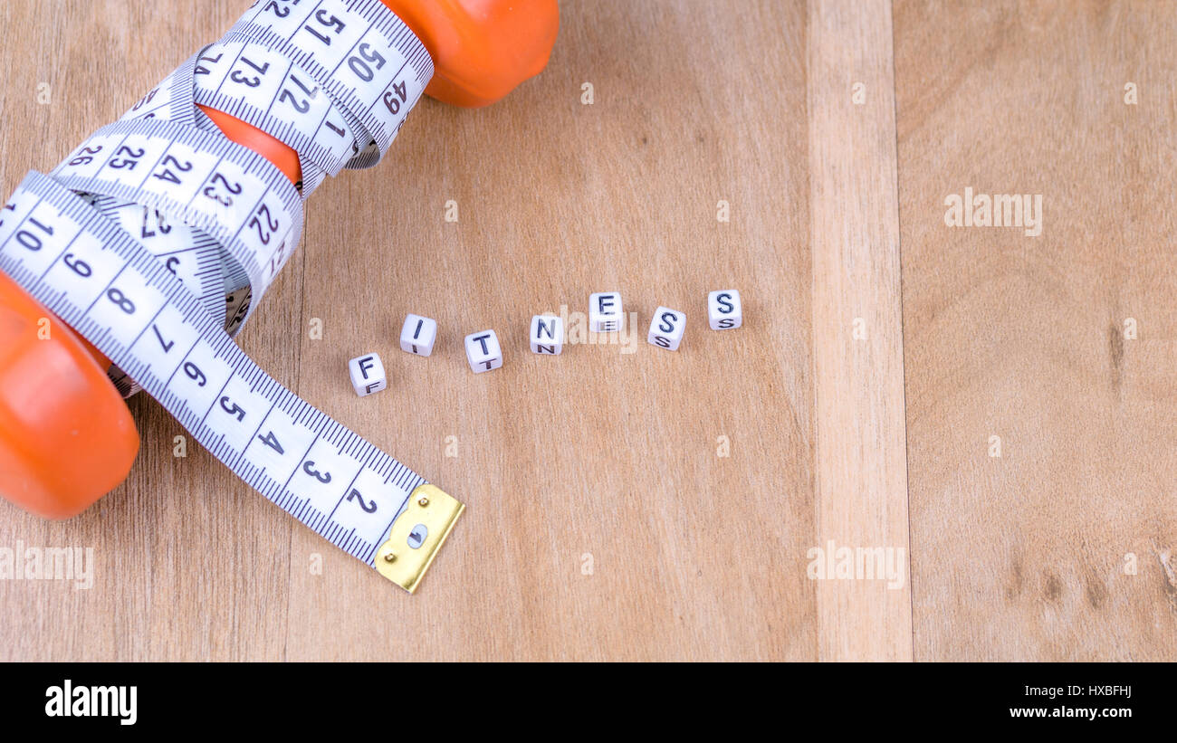 Orange dumbbell with centimetric tape and fitness cube letters on ...