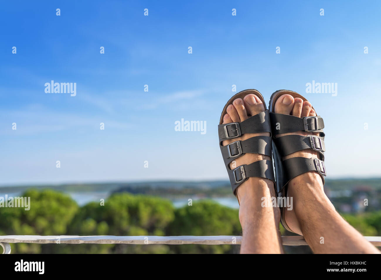 Male feet in leather slippers relaxing on balcony of summer vacation ...