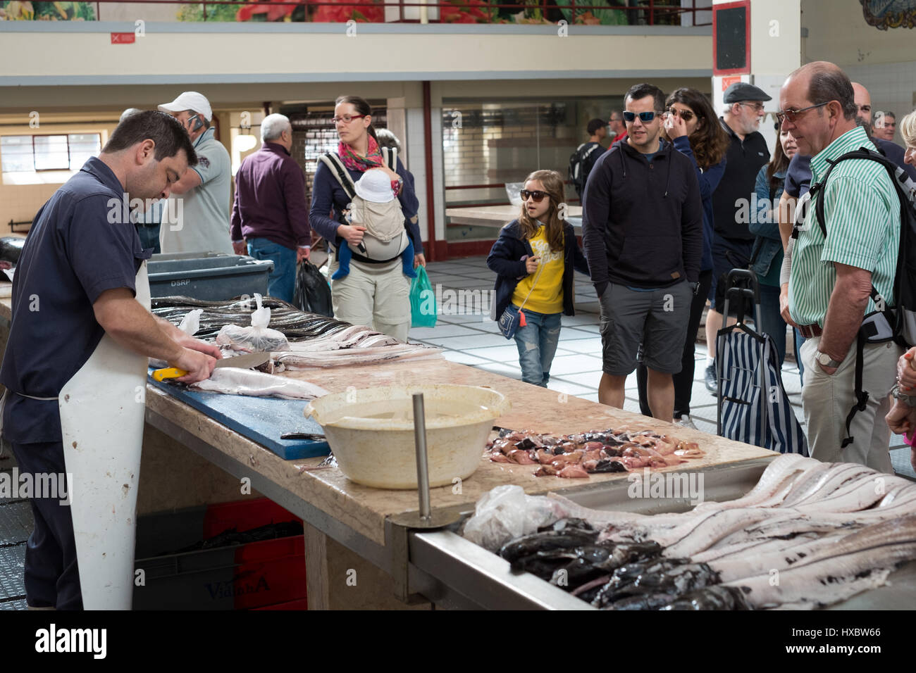 Tourists watch a fishmonger prepare a black scabbard fish into fillets ...