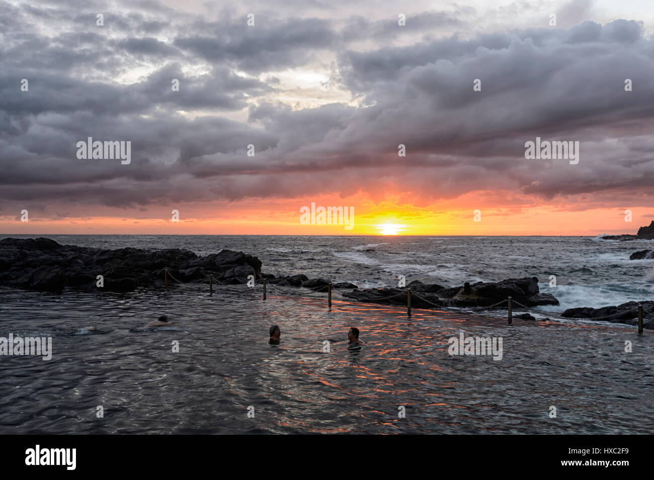 People swimming in front of a fiery sunrise over Kiama rock pool, Kiama ...