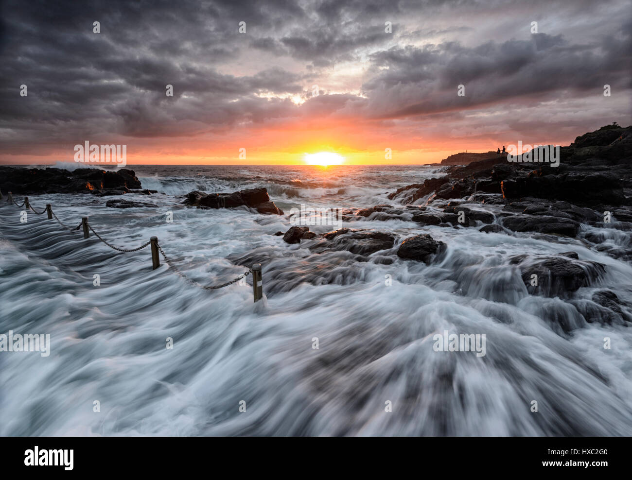 Heavy seas with large waves and a pink sky at sunrise over Kiama Rock ...
