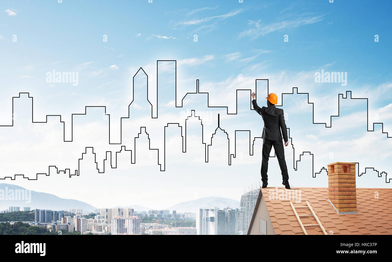 Engineer man standing with back on house roof and drawing city. Mixed ...