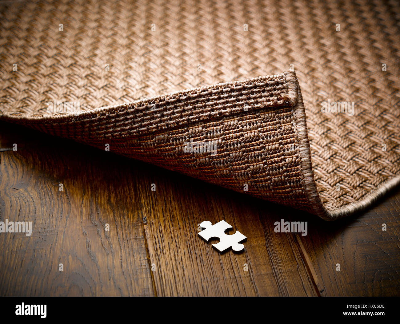 Puzzle piece hidden underneath rug Stock Photo - Alamy