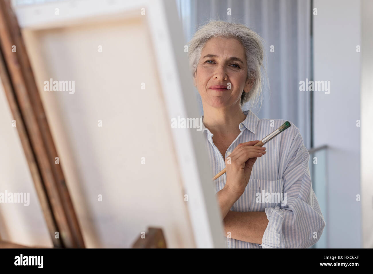 Portrait confident mature woman painting at canvas on easel Stock Photo ...