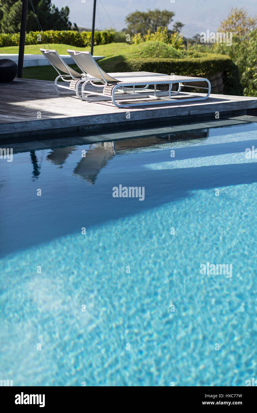 Sunny, tranquil blue swimming pool and lounge chairs Stock Photo - Alamy
