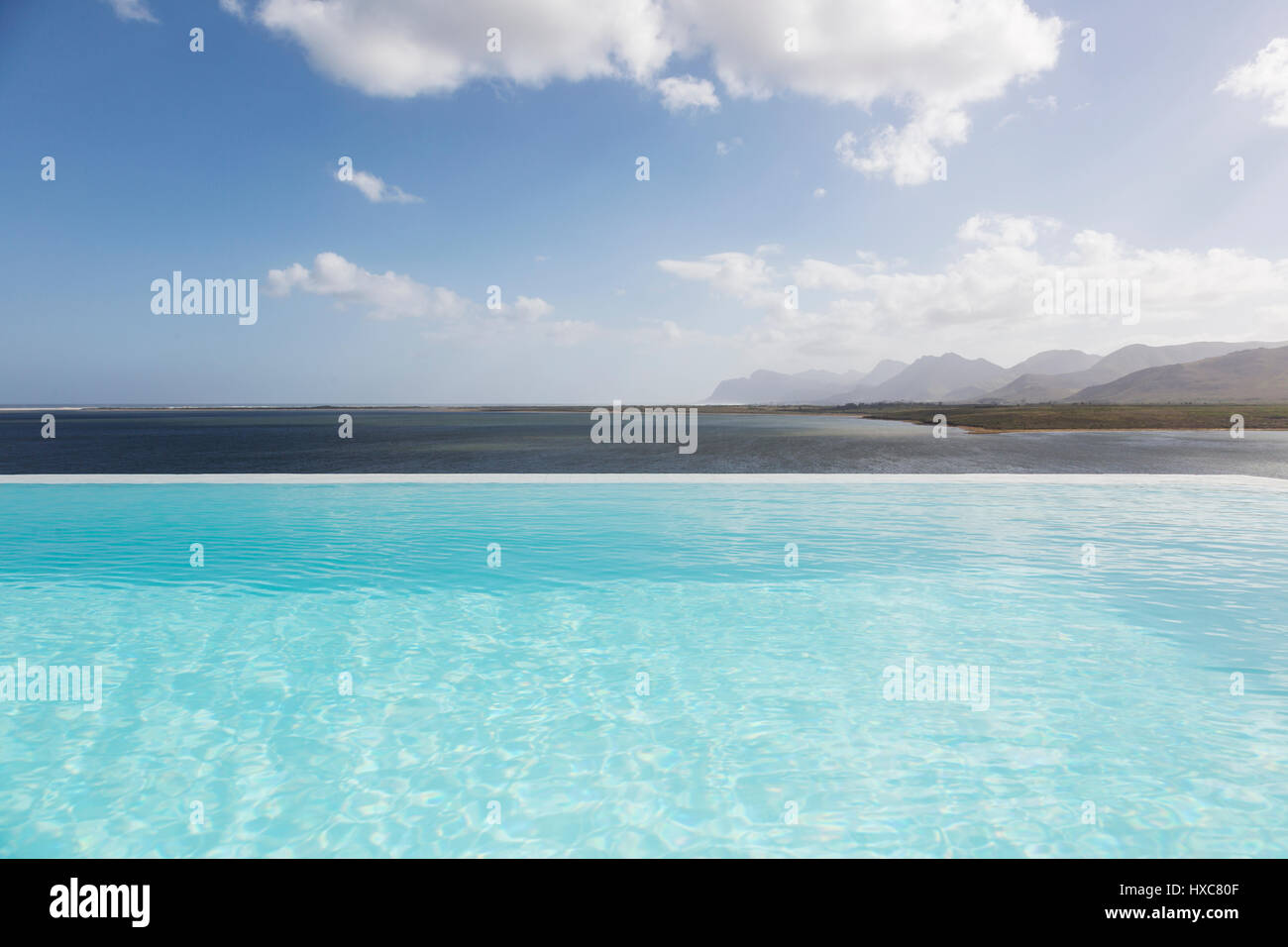Sunny, tranquil infinity pool with ocean view under blue sky with ...