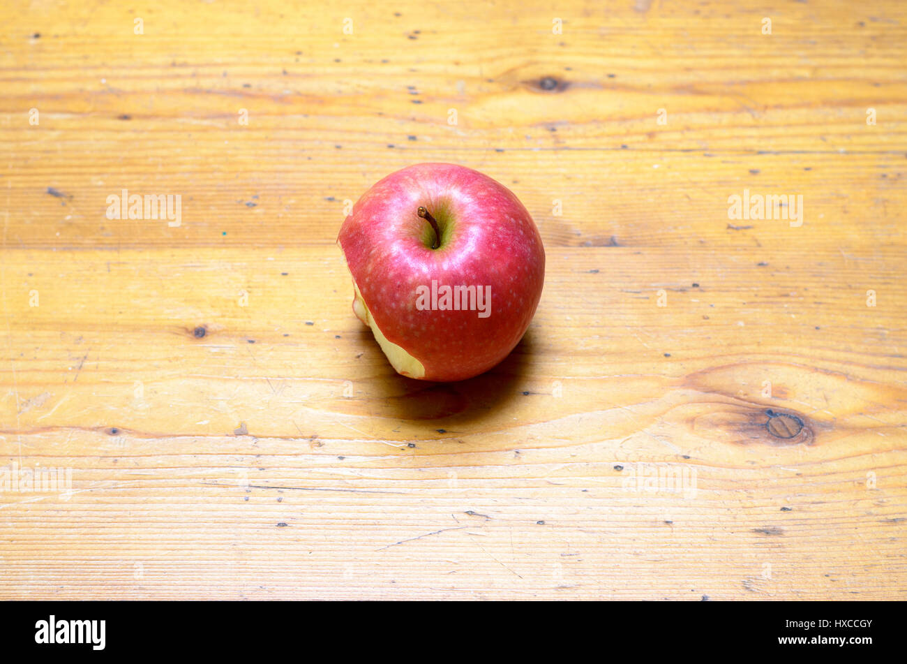 Partially eaten ripe red apple with bite marks centered on a wooden ...