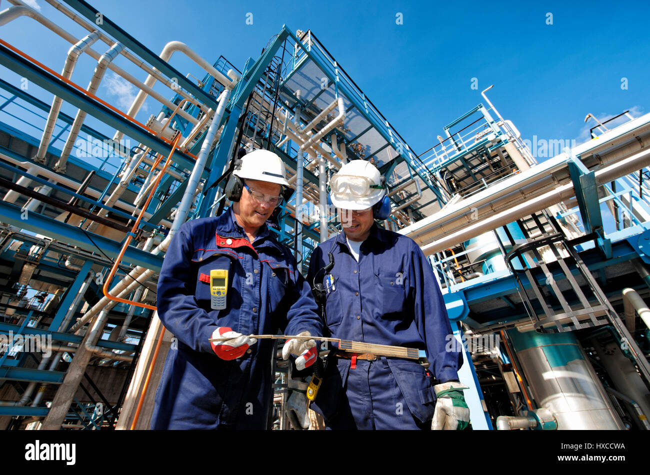 two refinery workers with large pipelines construction in background ...
