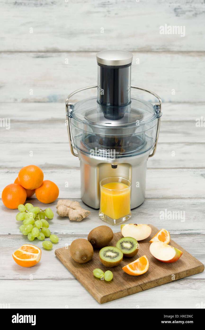 Modern electric juicer, various fruit and glass of freshly made juice ...